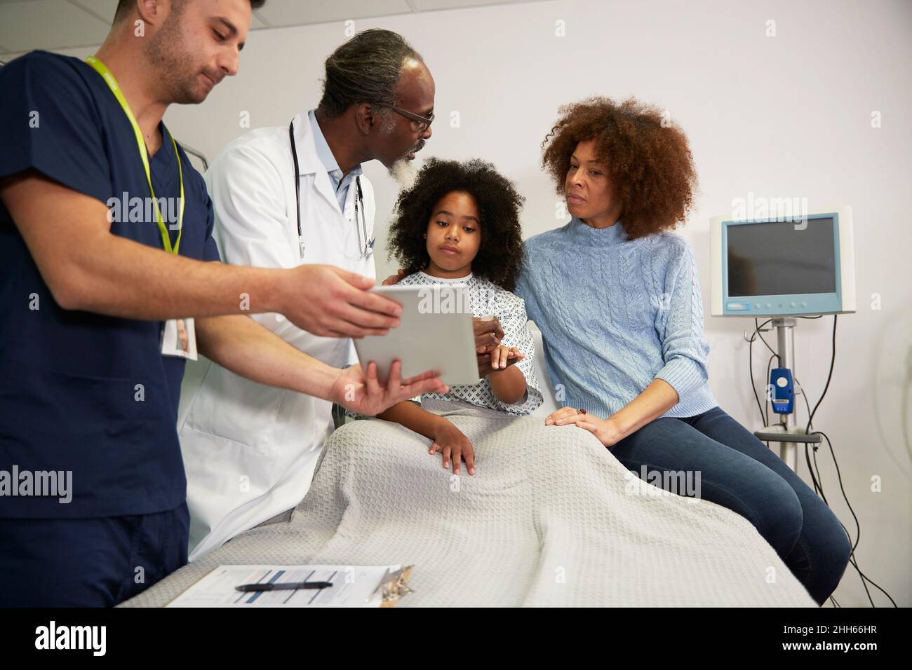 Male nurse holding tablet PC in front of patient sitting on bed at ...