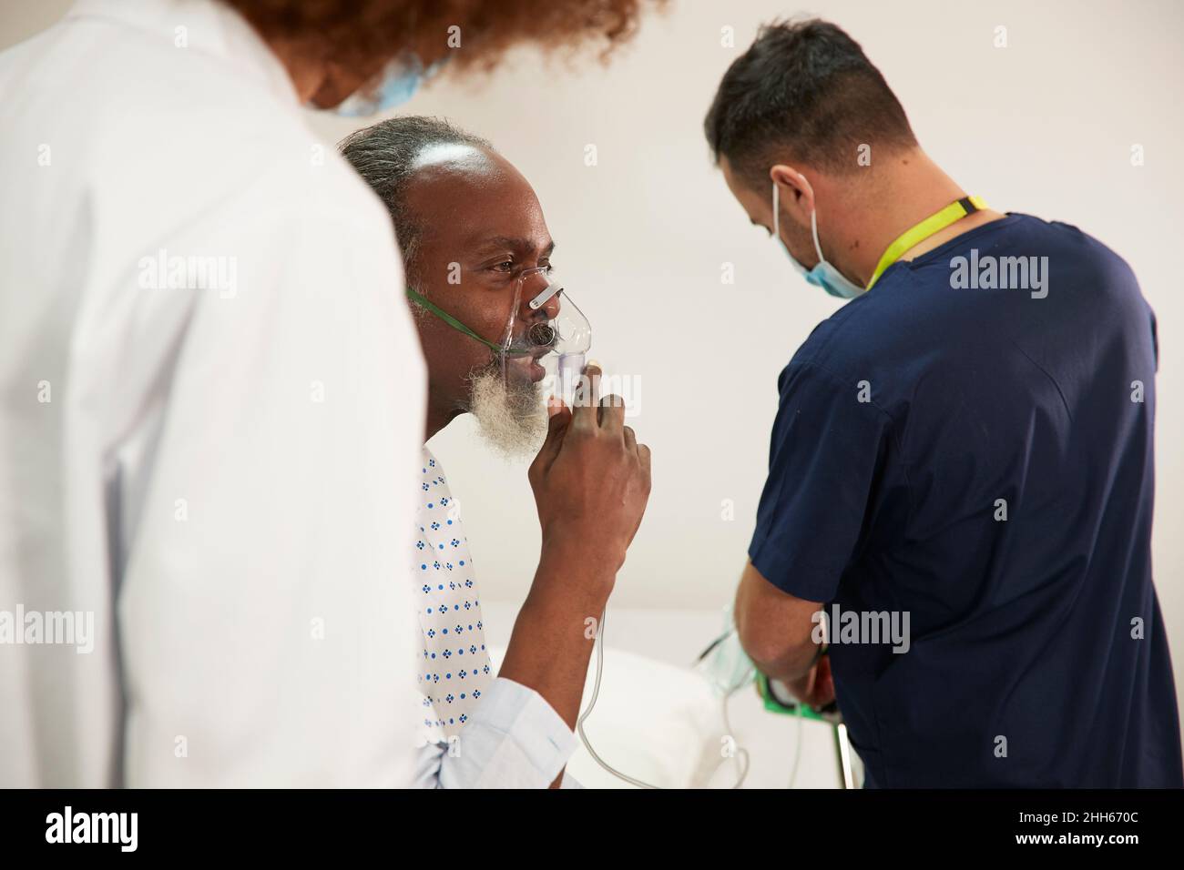 Patient wearing oxygen mask with healthcare workers in medical room ...