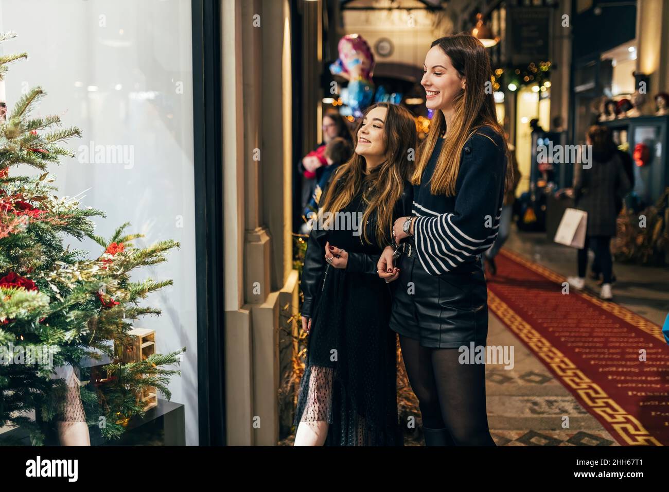 Smiling friends looking at Christmas tree through store window at night ...