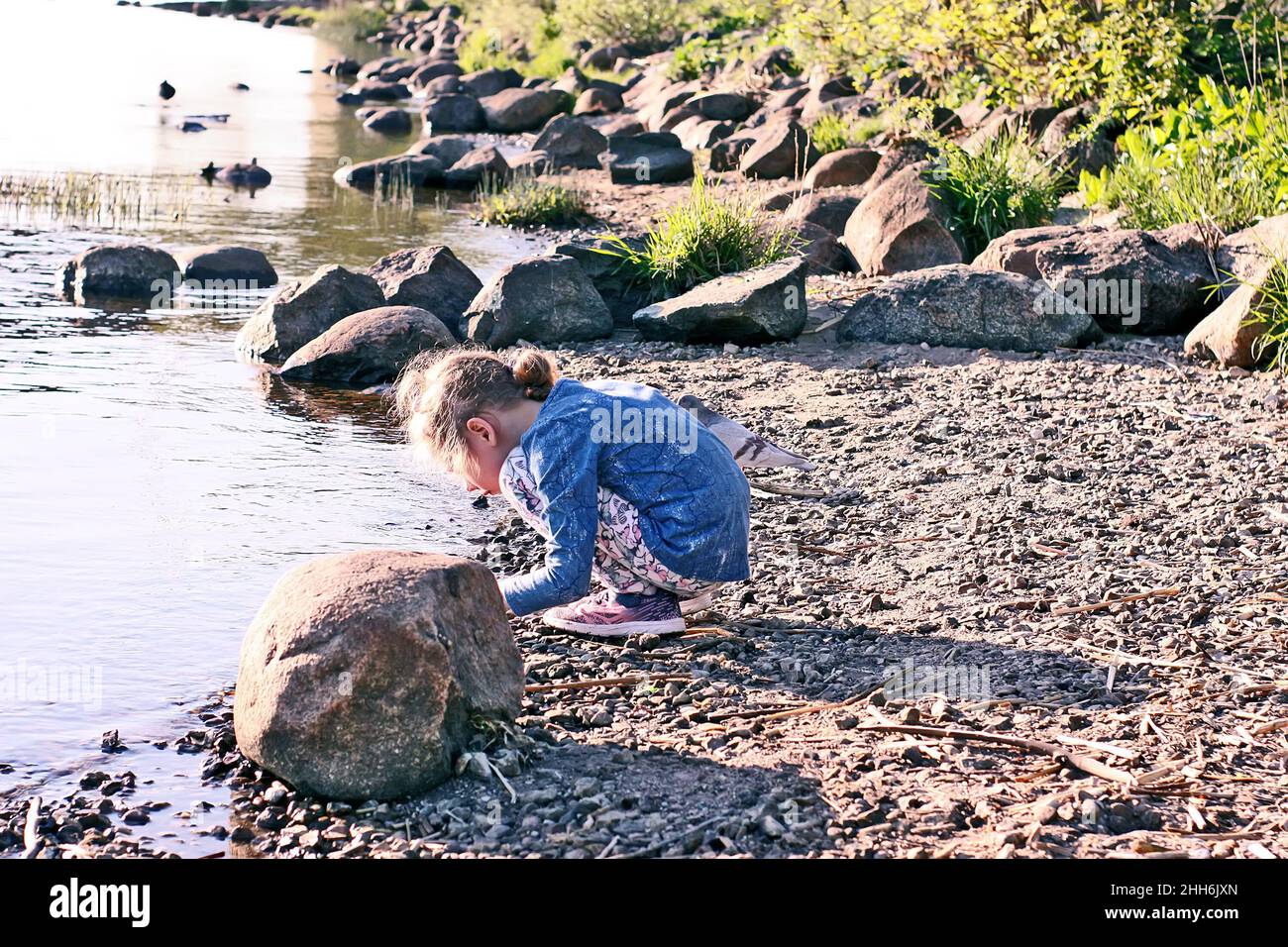 Adorable little girl playing with small stones on the river coast at ...