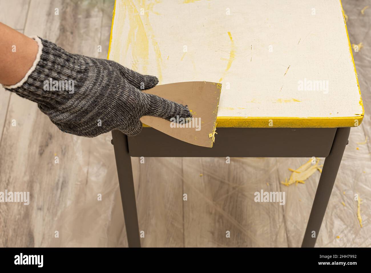 a hand with a paint scraper removes a layer of paint from a stool. High ...