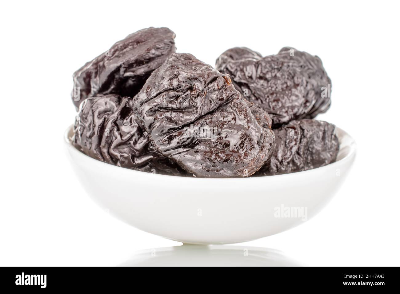 Several organic sweet prunes on a white ceramic saucer, macro, isolated ...