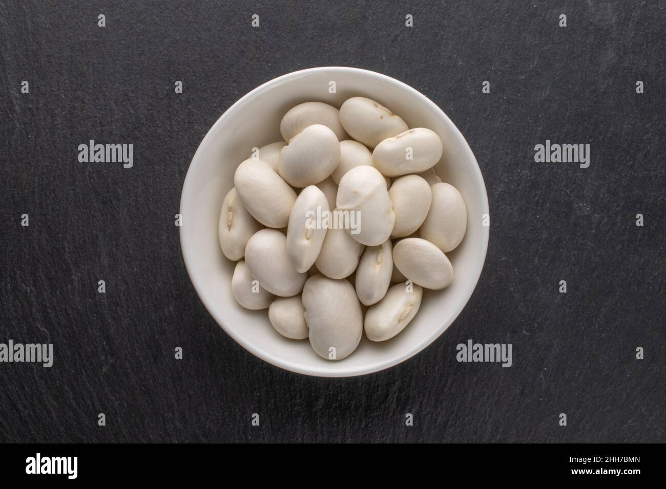 Dried grains of organic white beans in a ceramic dish on a slate board ...
