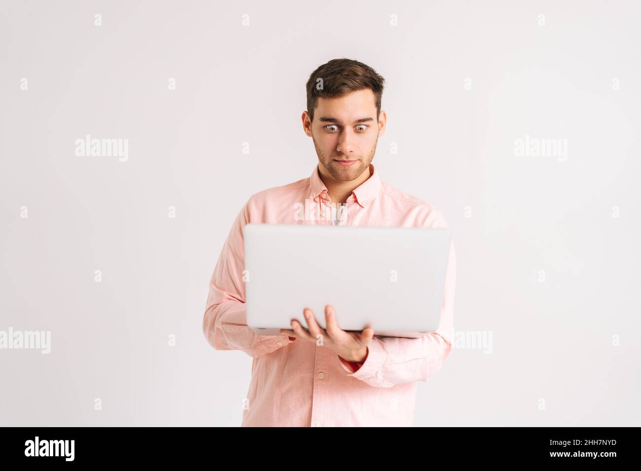 Portrait of shocked young man standing with laptop looking on screen ...