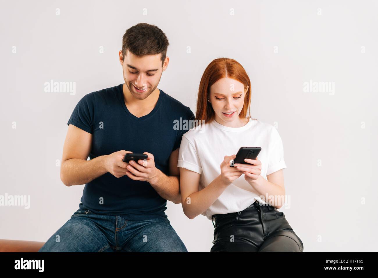 Studio portrait of happy addicted couple using browsing mobile phone ...