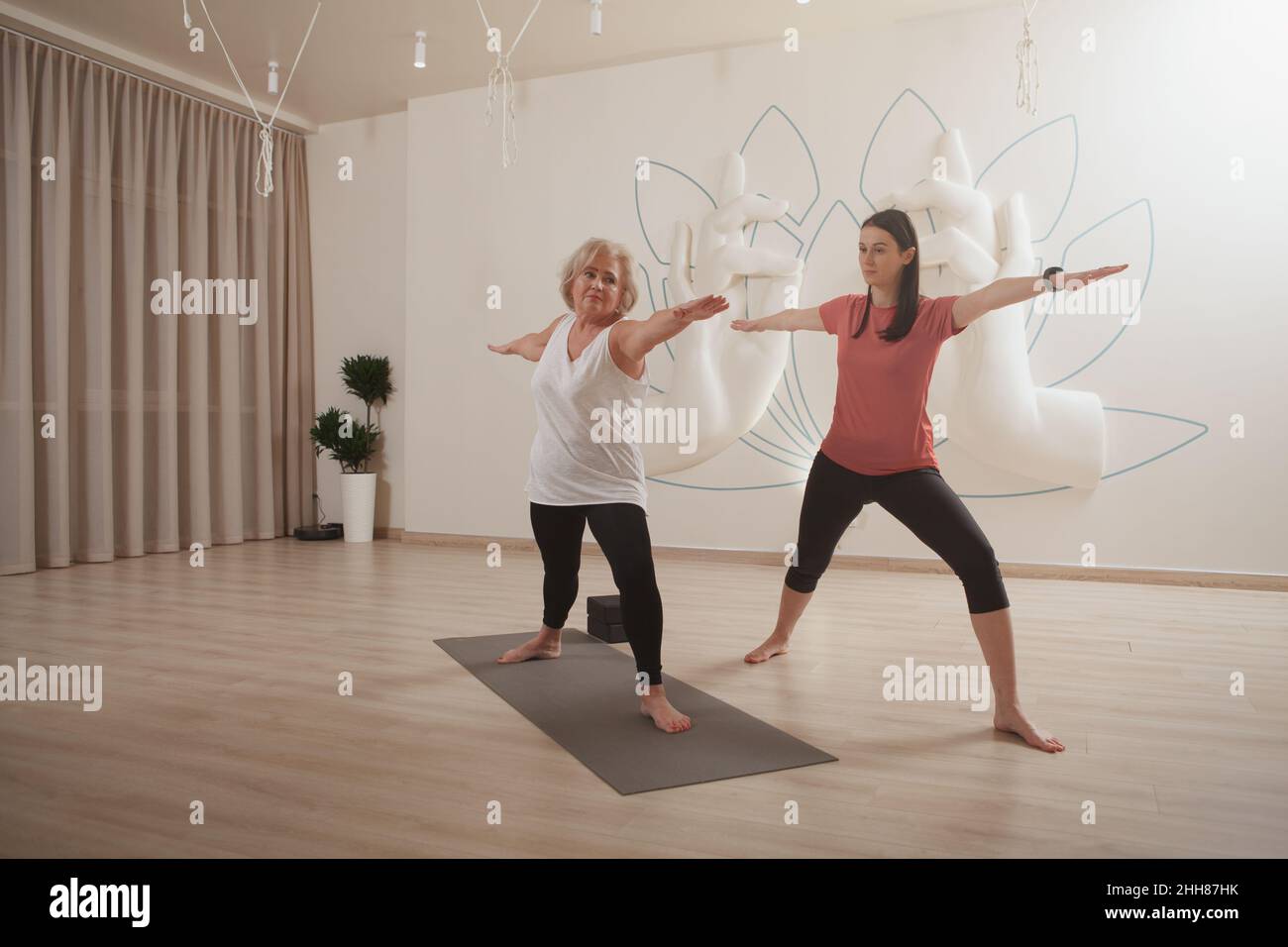 Cheerful senior woman enjoying yoga class with personal trainer, doing ...