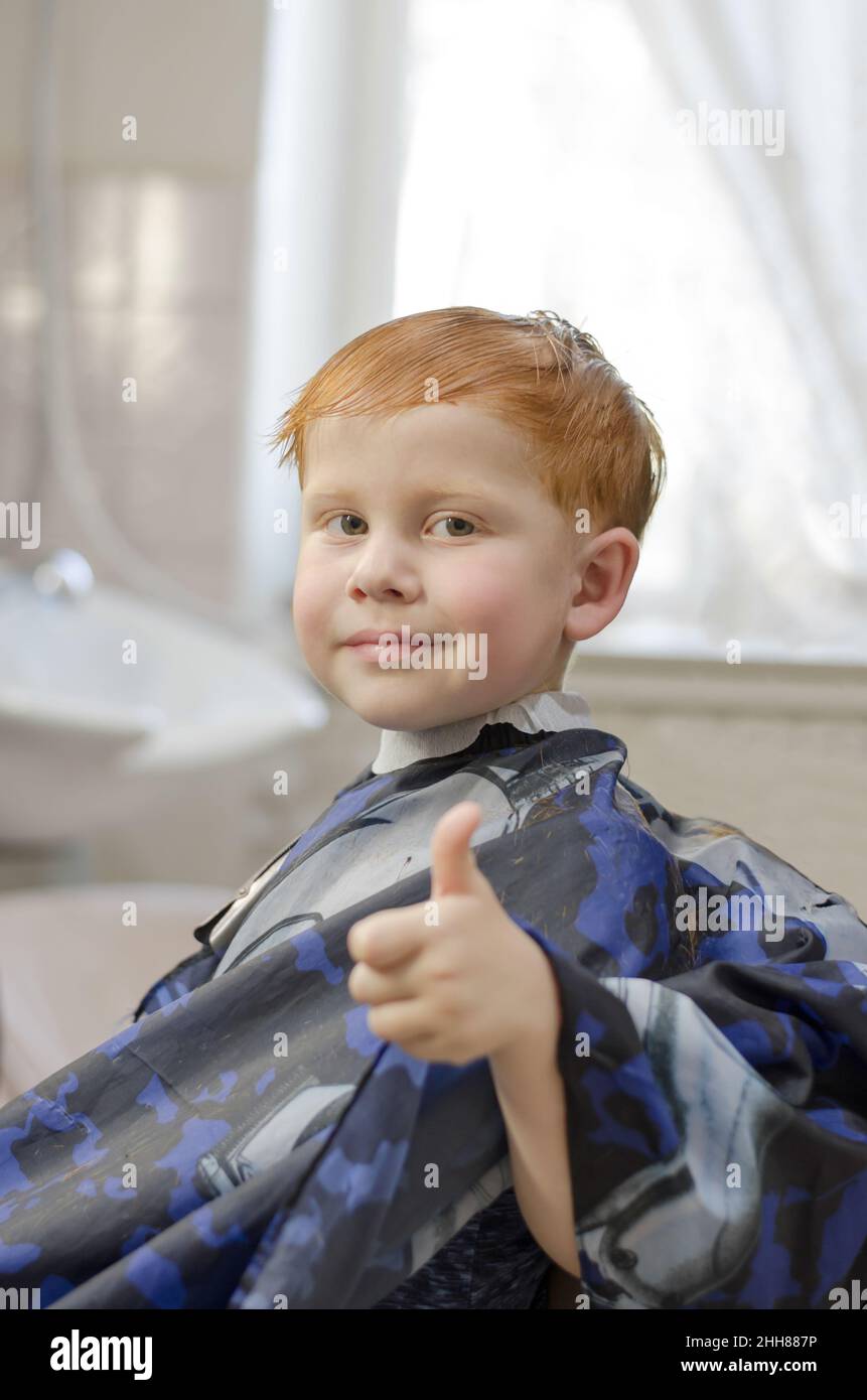 Red-haired four-year-old boy smiling at the barbershop. Joyful child in ...