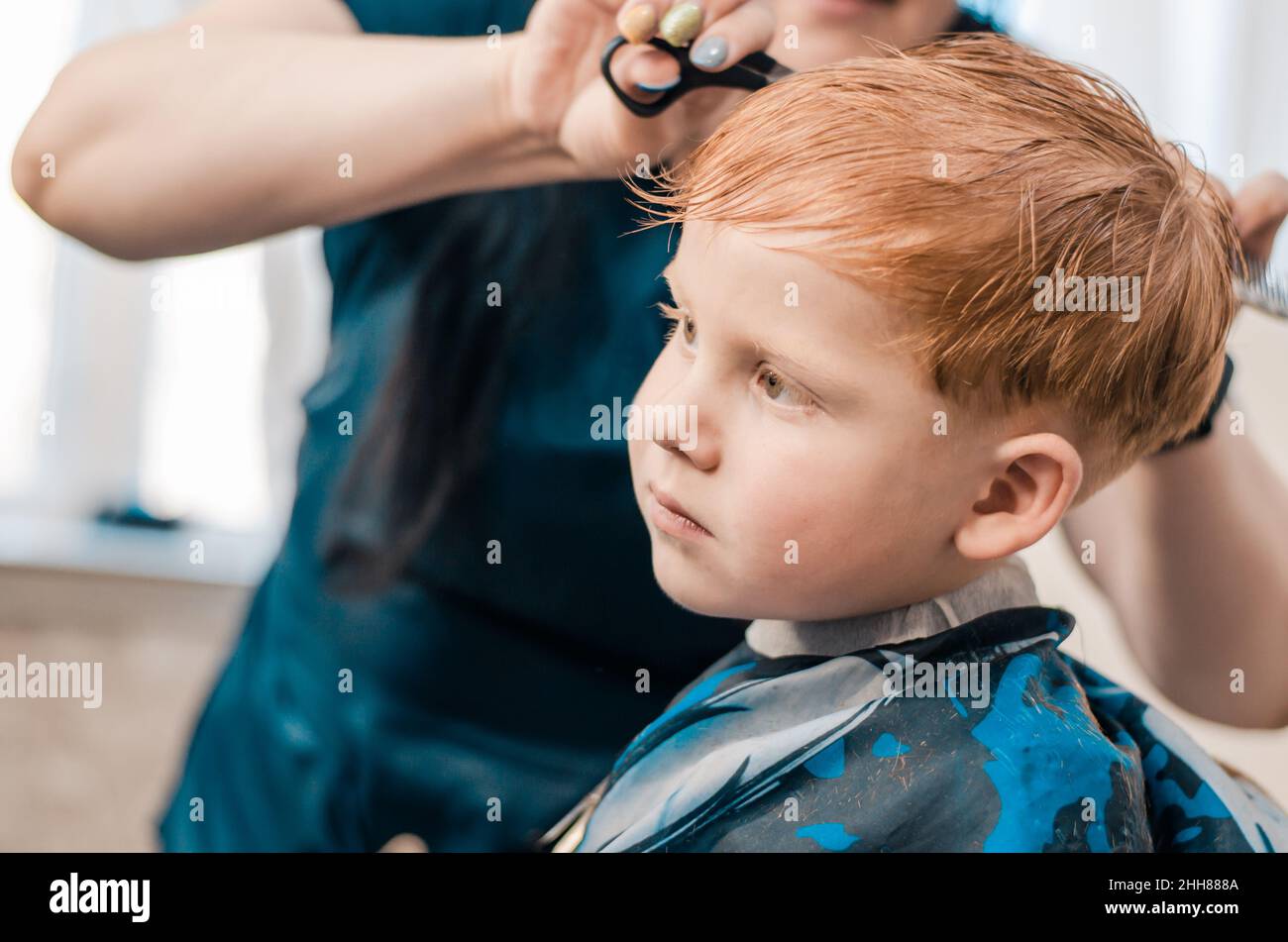 4 year old redhead boy at the barbershop. Hairdresser cuts a child's ...