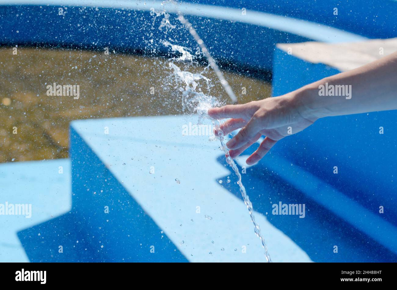 A woman's hand touches the cool water in the fountain. Hot summer ...
