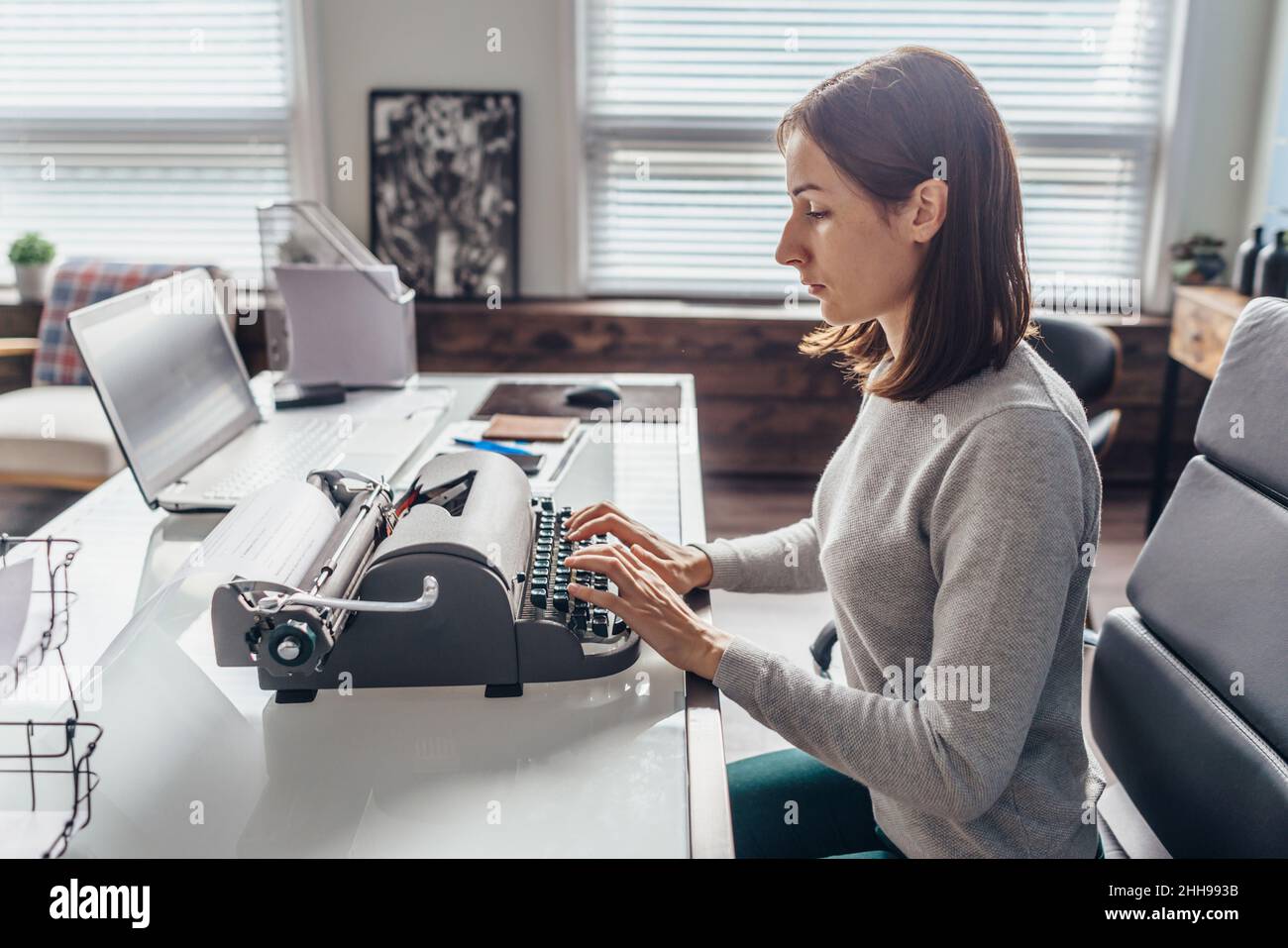 Woman author composes text on a typewriter sitting in her working room ...