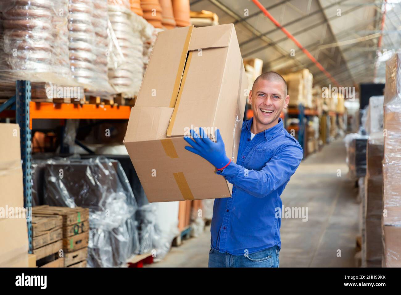 Positive warehouse worker dragging boxes on hands Stock Photo - Alamy