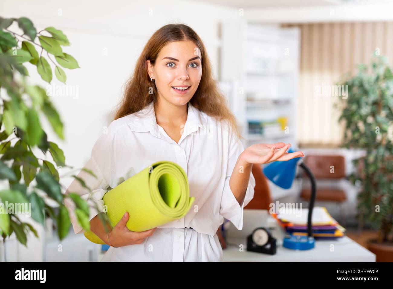 Portrait of a young girl standing in the office, holding a tourist mat ...