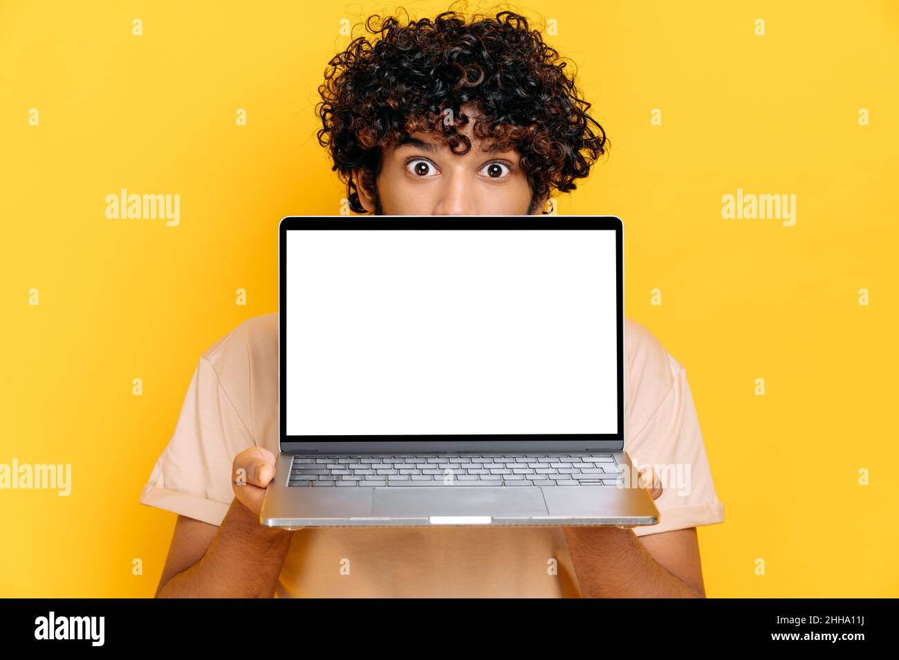 Amazed excited young Indian man peeking out from behind laptop, looks ...