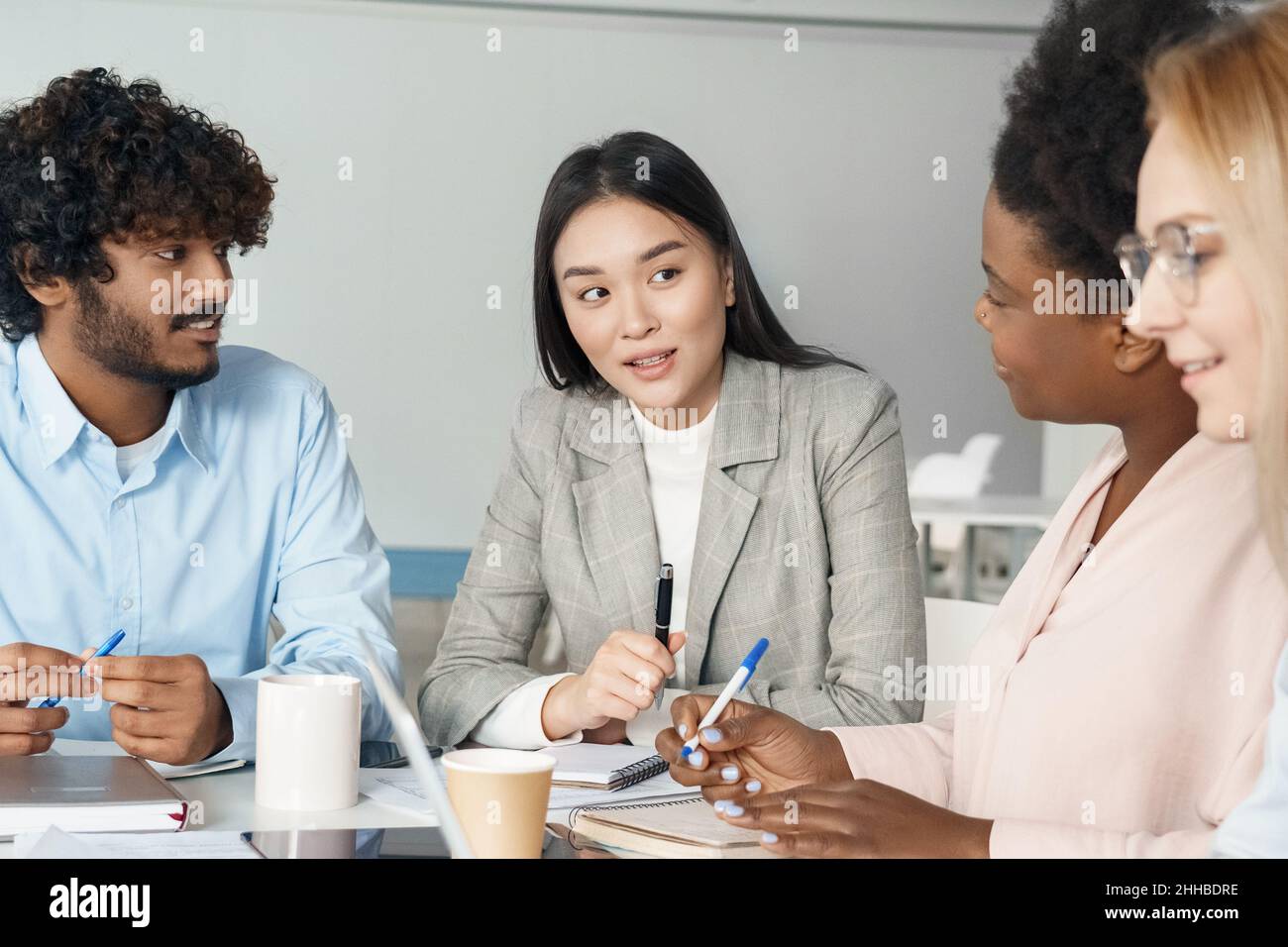 Multi-ethnic diverse students working on common project sitting at desk ...