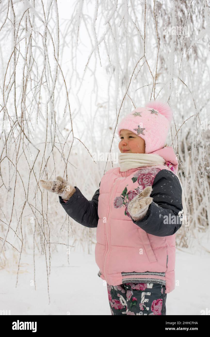 Blissful female kid with red cheeks looking at tree branches and ...