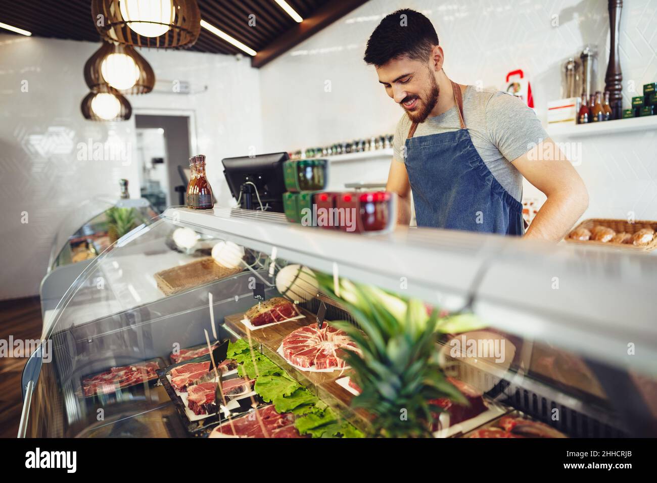 Young man butcher arranging meat products in display case of butcher ...