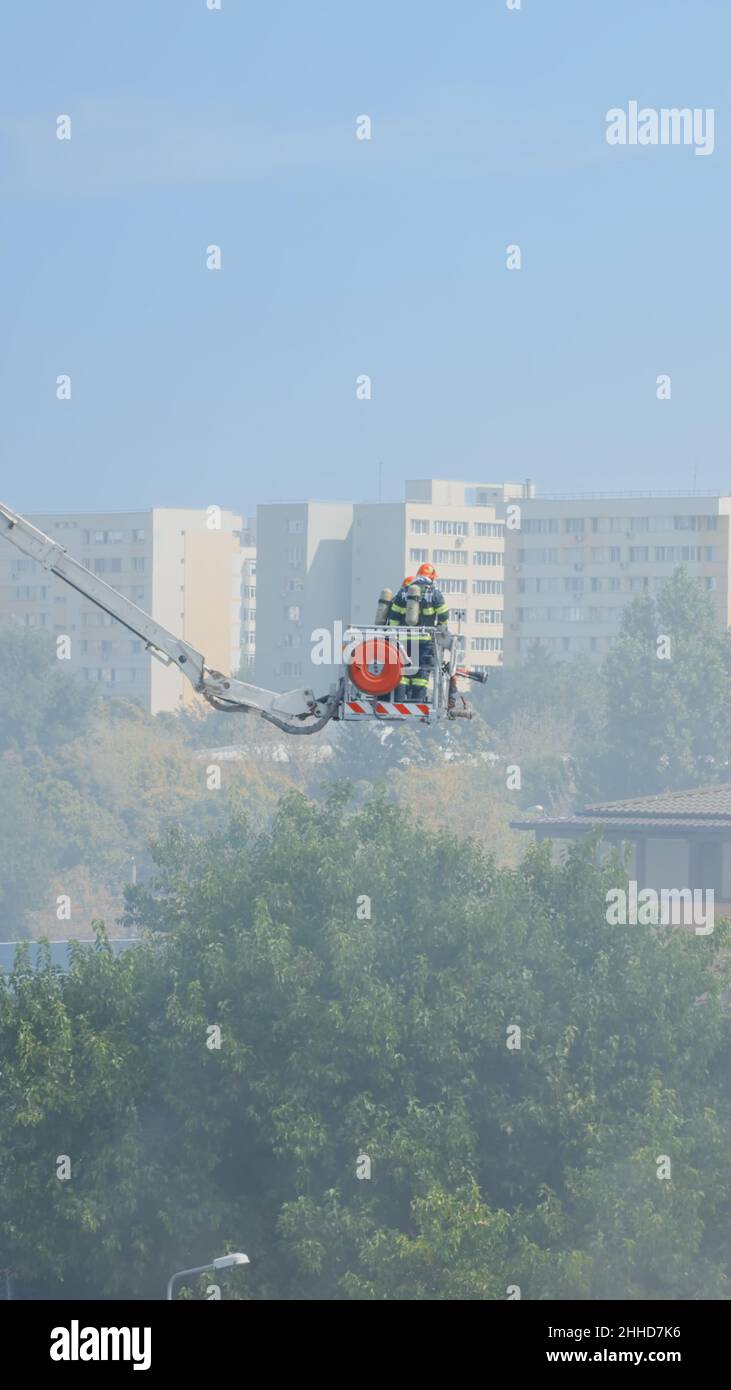 Firemen on platform truck going on roof of house on fire. View of ...
