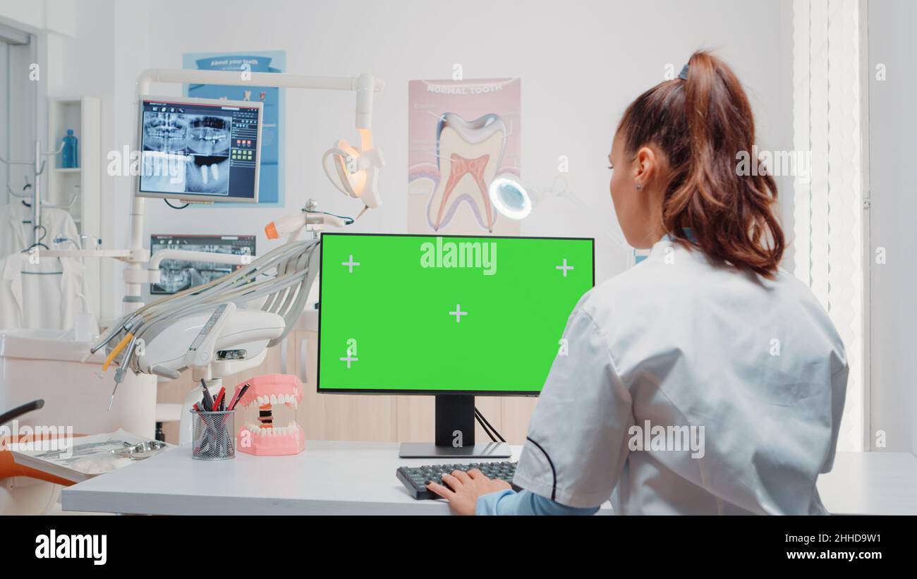 Woman using keyboard and computer with green screen in dental cabinet ...