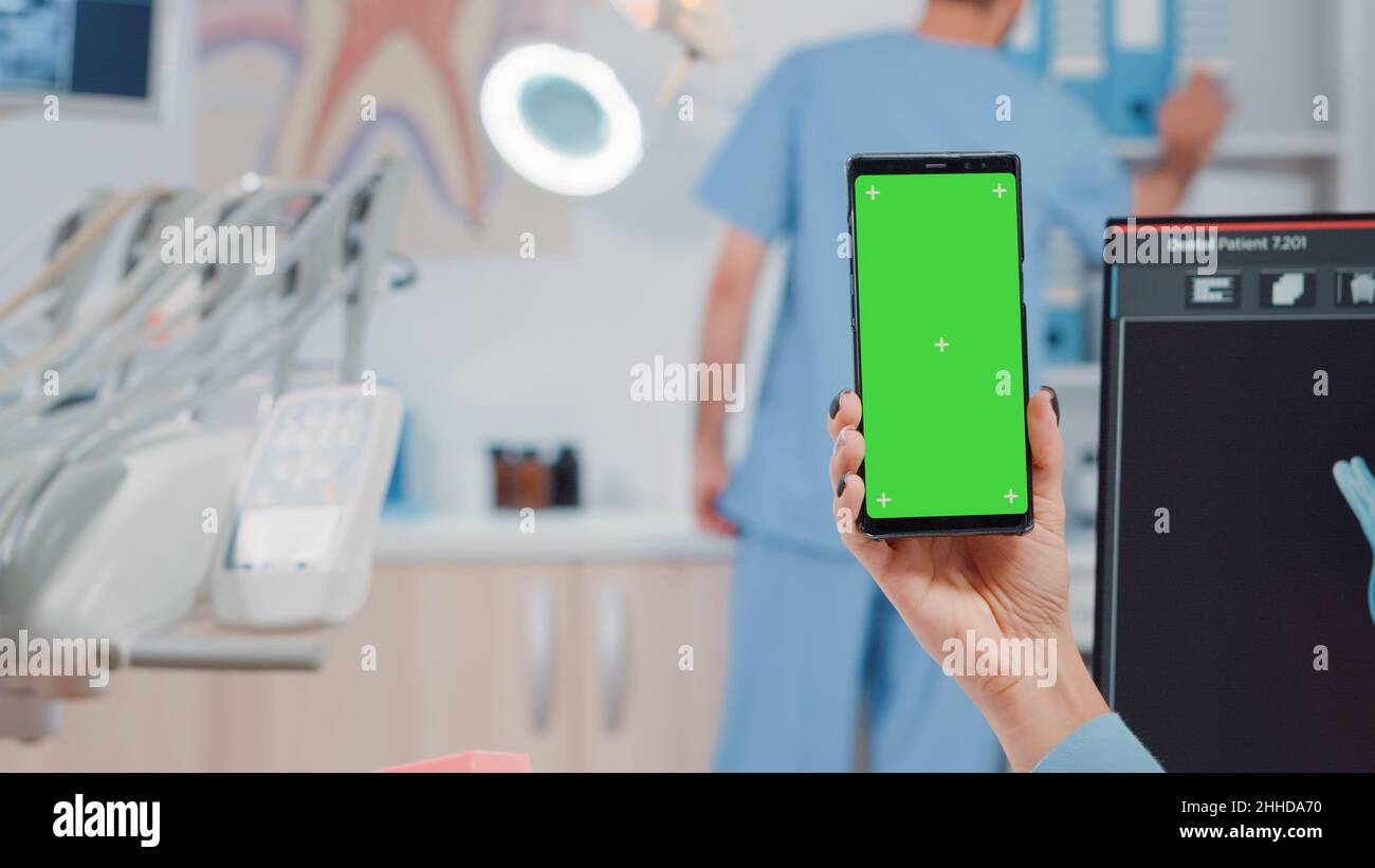 Close up of dentist holding smartphone with green screen for teethcare ...