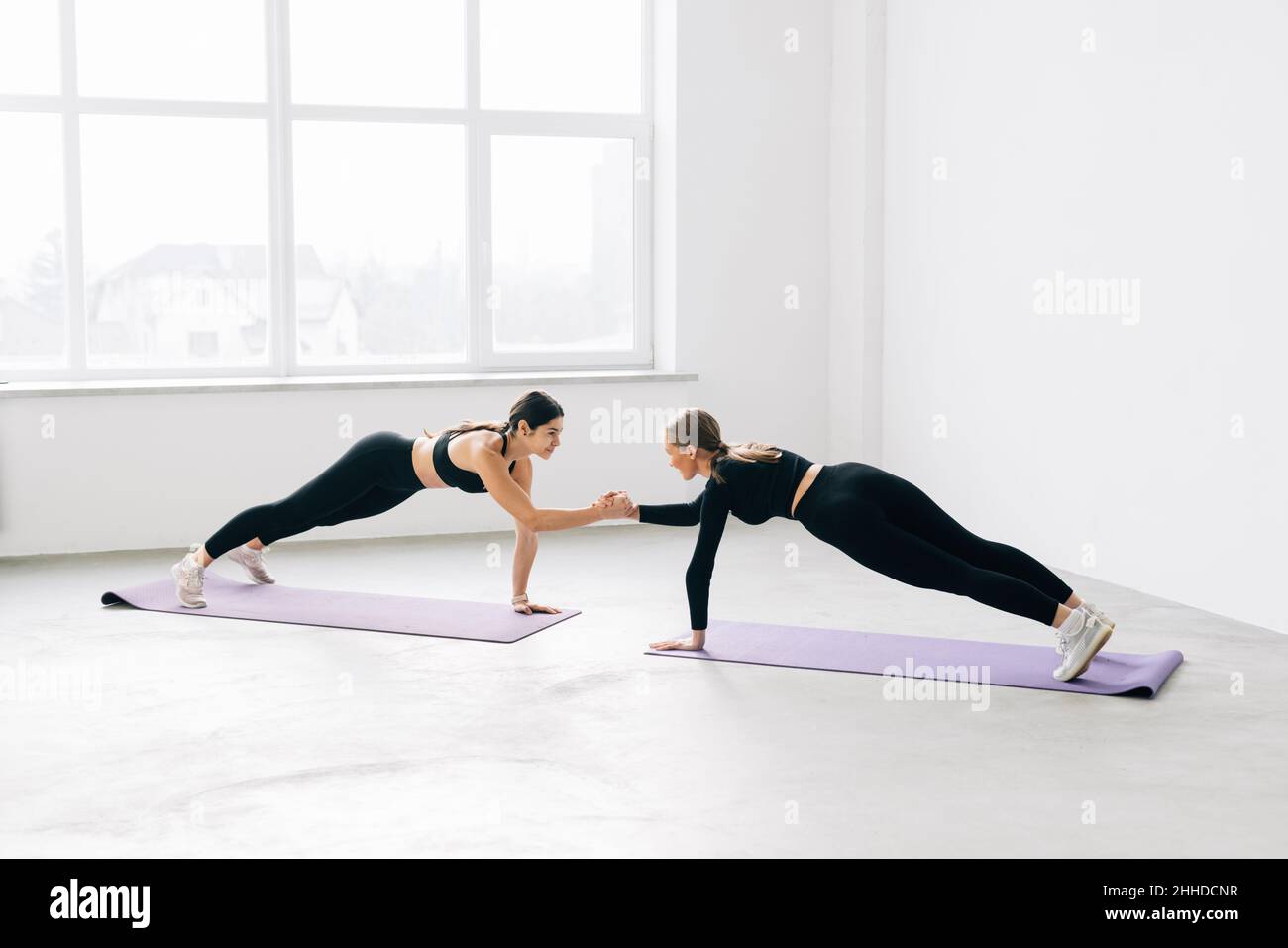 Two young beautiful women giving high five while practicing basic plank ...