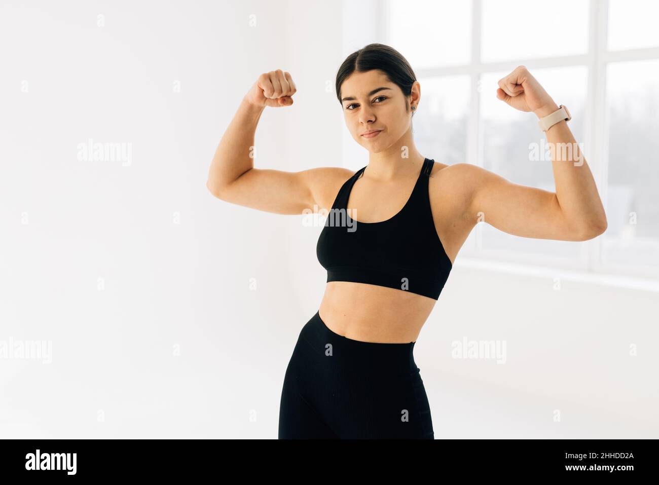 Cheerfully sporty woman demonstrating biceps, isolated on white ...
