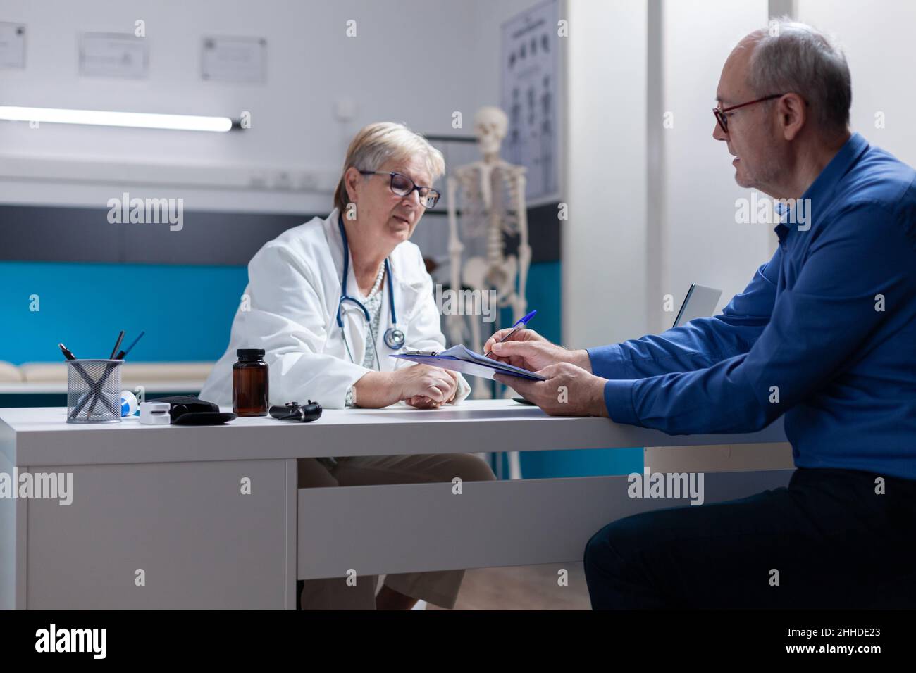 Patient signing checkup papers for physician at examination appointment ...
