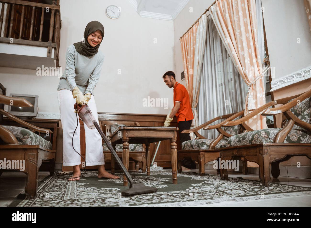 Veiled mother uses a vacuum and dad mops while cleaning Stock Photo - Alamy