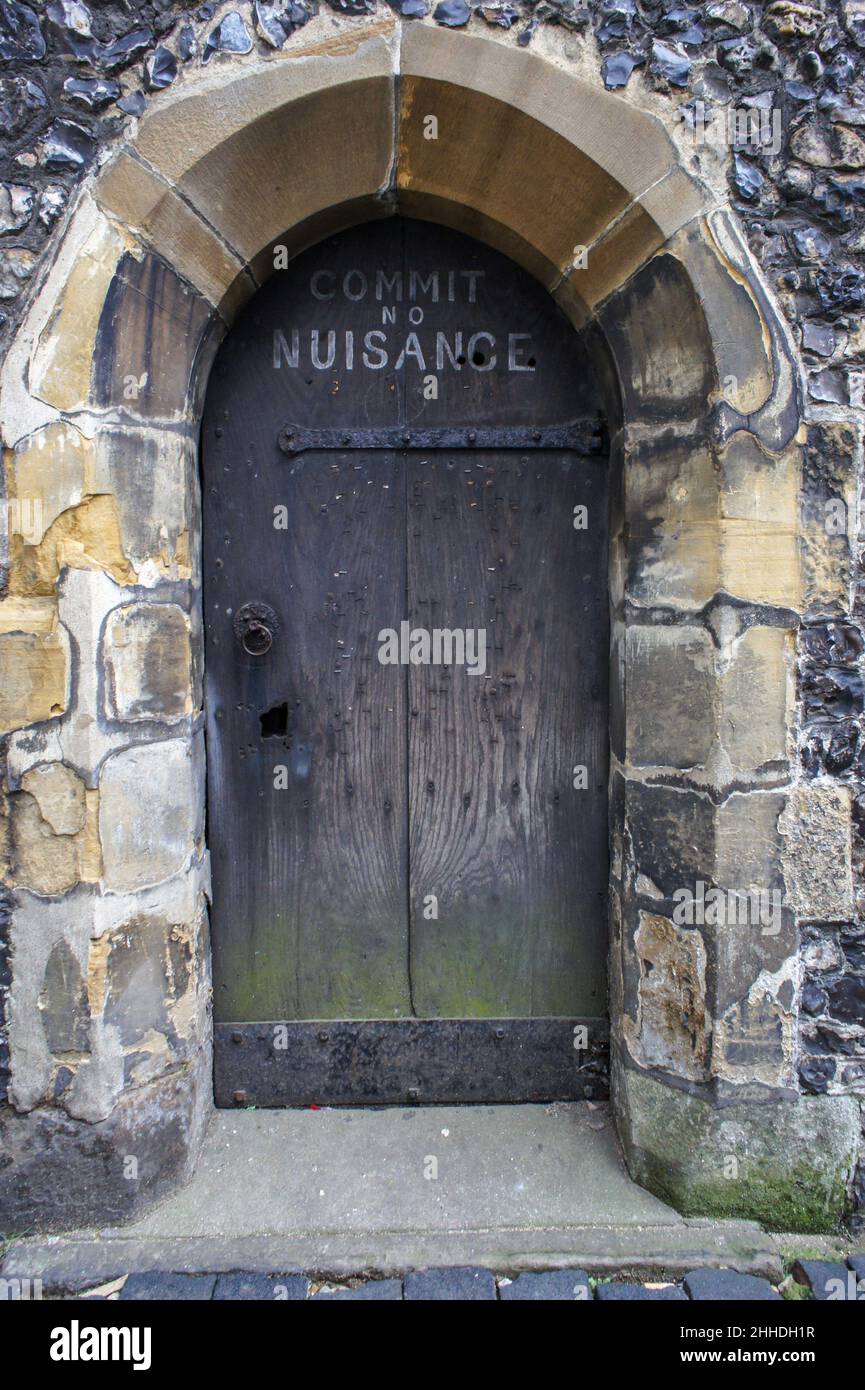 Small wooden door with the sign Commit No Nuisance on the ancient clock ...