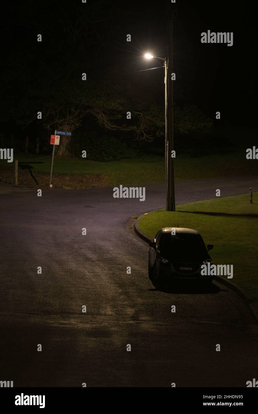 A car parked under a single isolated street light on a road on a dark ...