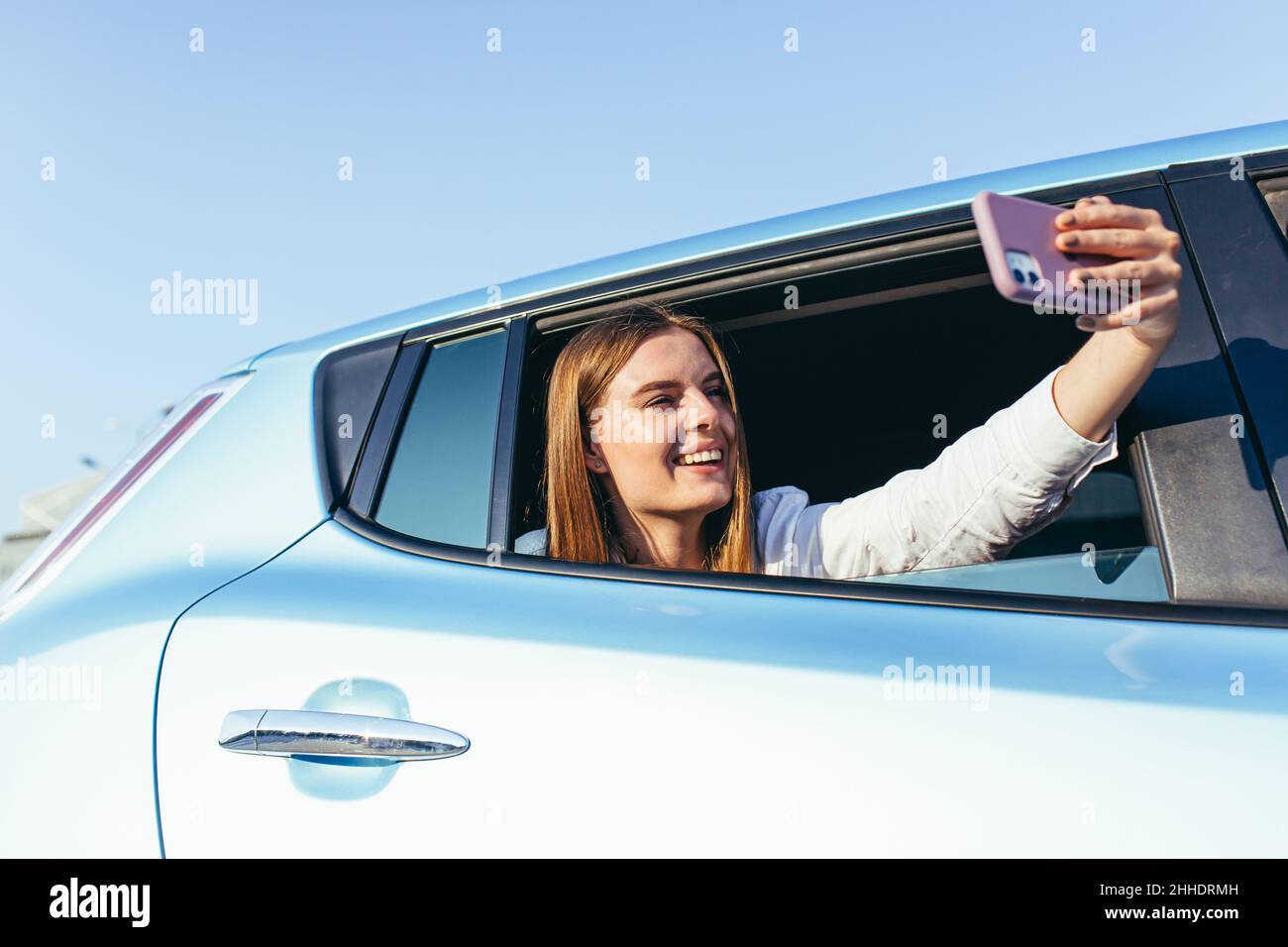 Young beautiful woman talking on video call sitting in the car sticking ...