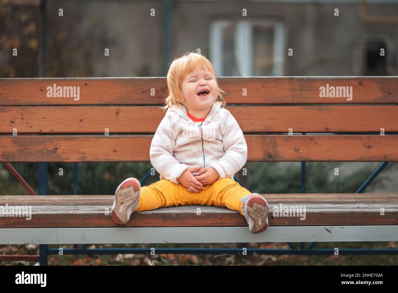 Childrens shelter. A cry little girl is sitting on a bench on the ...