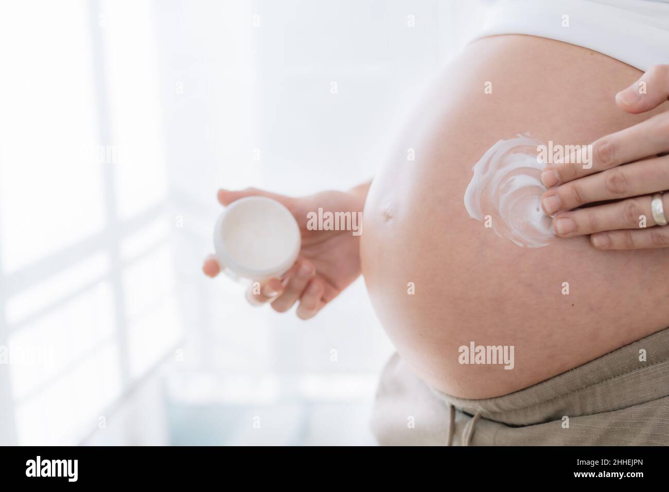 pregnant woman's hand applying moisturizing cream on the skin of her ...