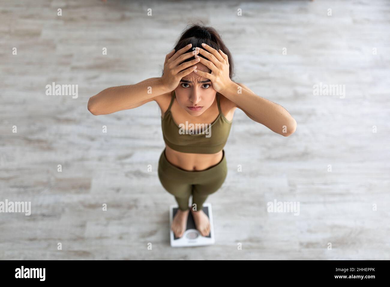 Terrified young Indian woman standing on scales, holding head in ...