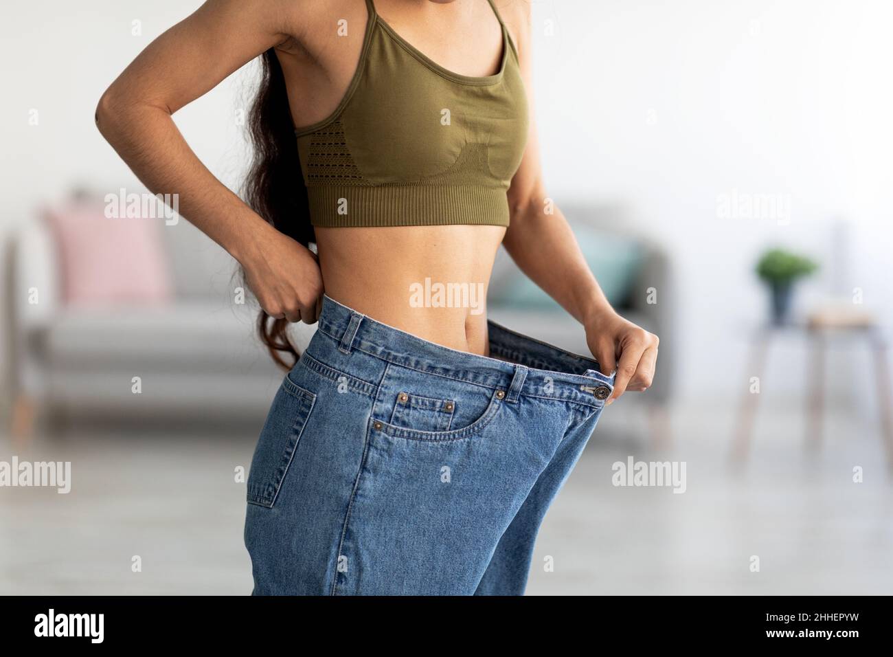 Successful weight loss diet. Closeup of young Indian lady in big jeans demonstrating results of ...