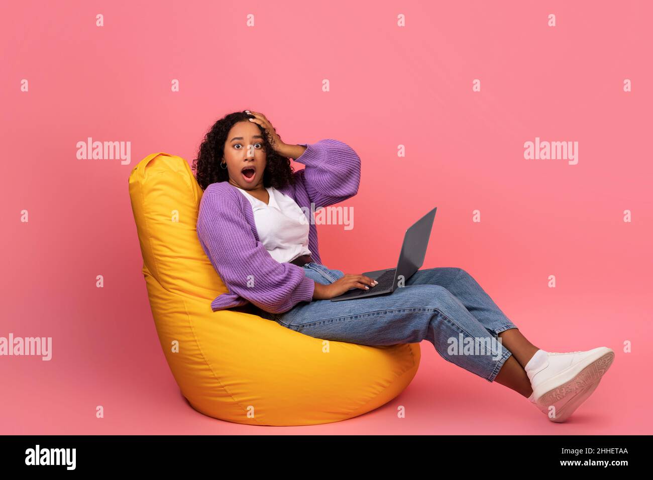 Portrait of shocked young black woman sitting in bean bag chair with ...