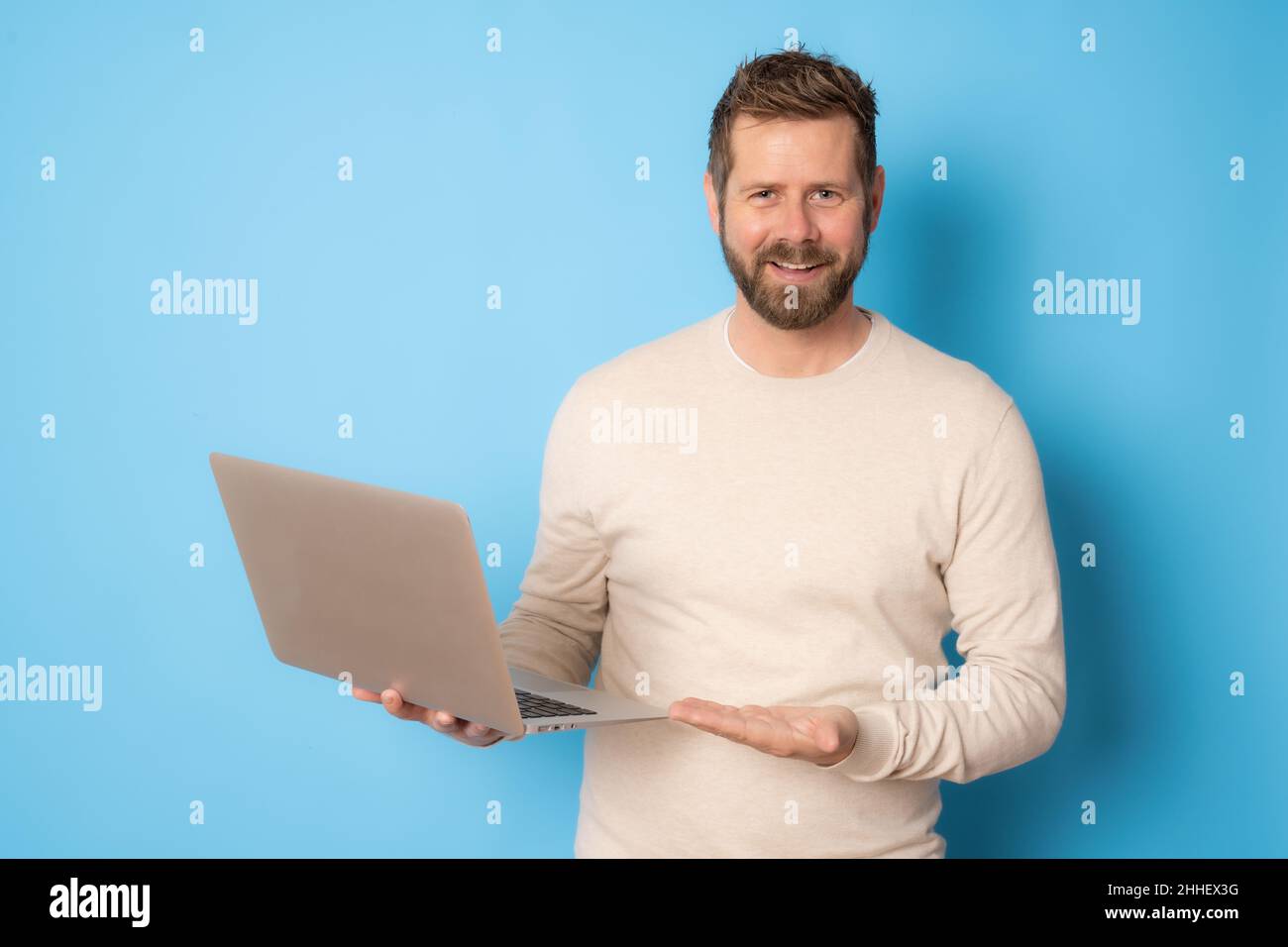 Young bearded man in casual clothing using laptop computer standing ...
