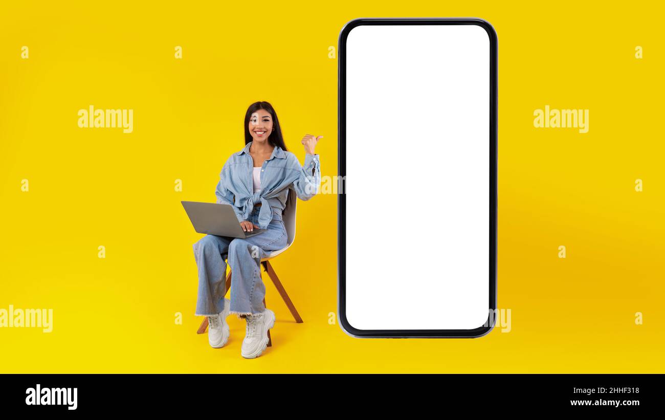 Happy lady using pc pointing at mobile phone screen Stock Photo - Alamy