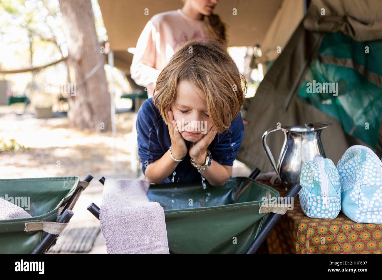 A boy washing his face in a basin at a campsite in the Okavango Stock ...