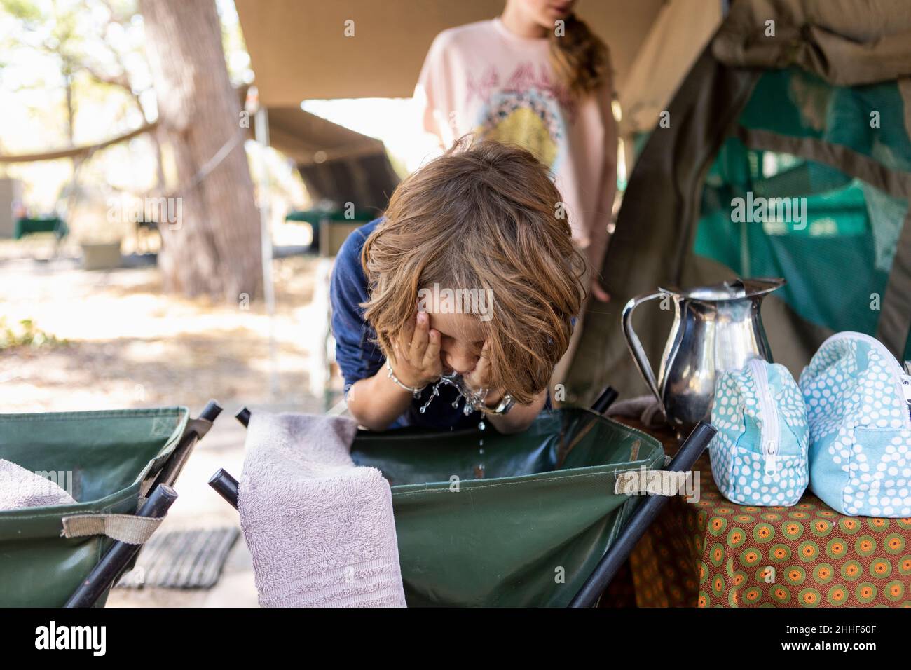 A boy washing his face in a basin at a campsite in the Okavango Stock ...