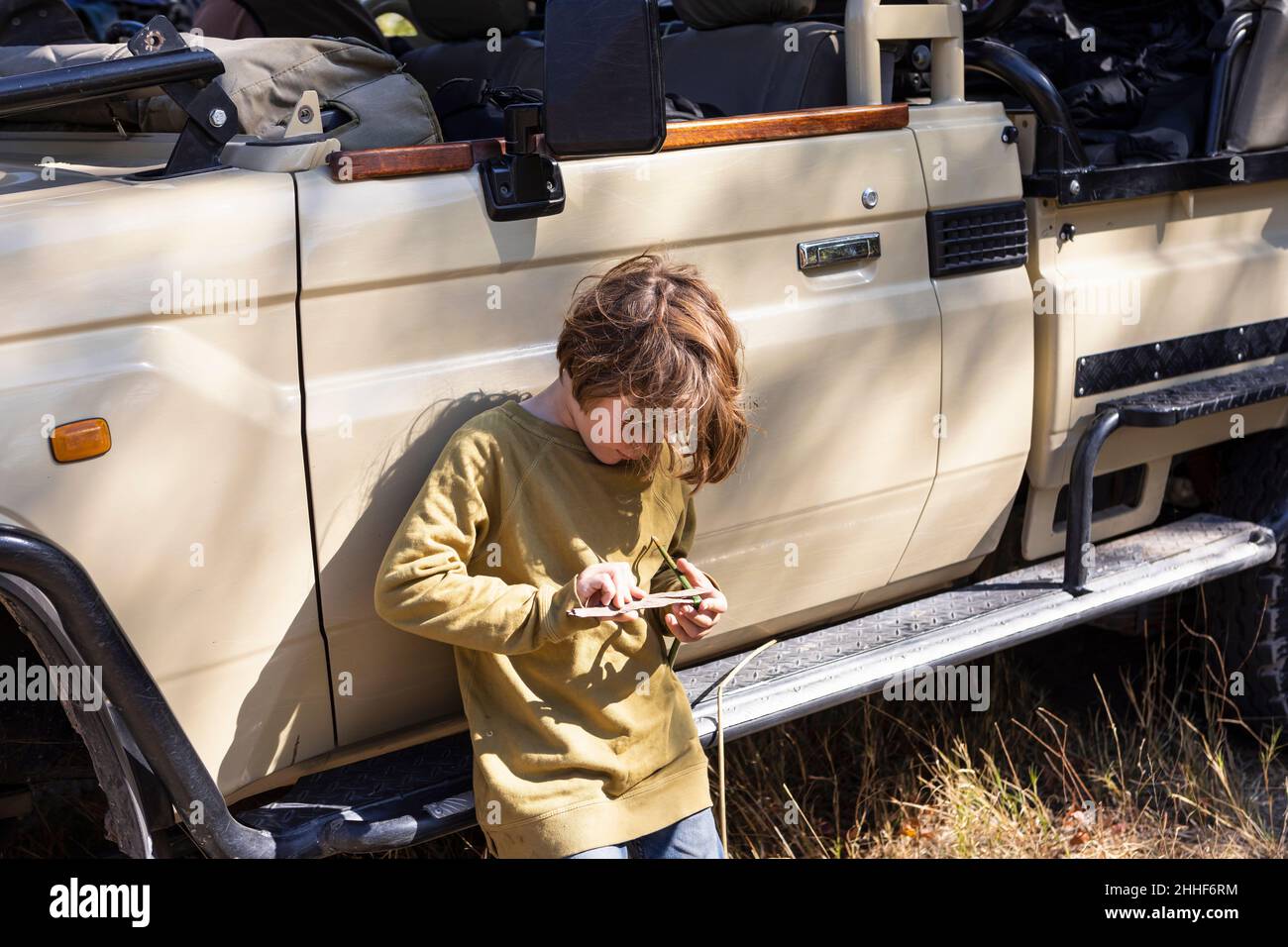 Eight year old boy leaning against a jeep, playing with a toy Stock ...