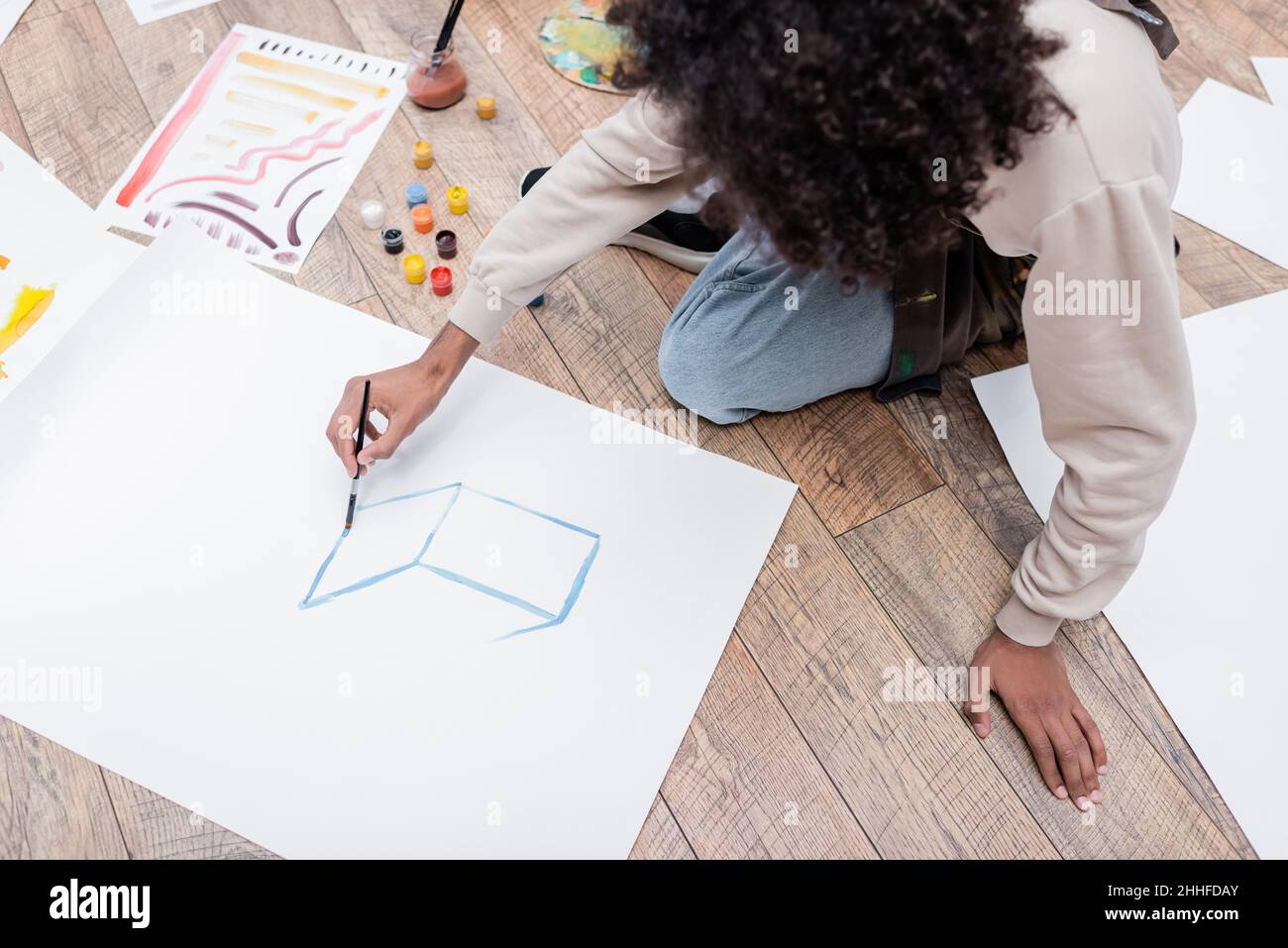 Overhead view of african american man painting on paper near paints on ...