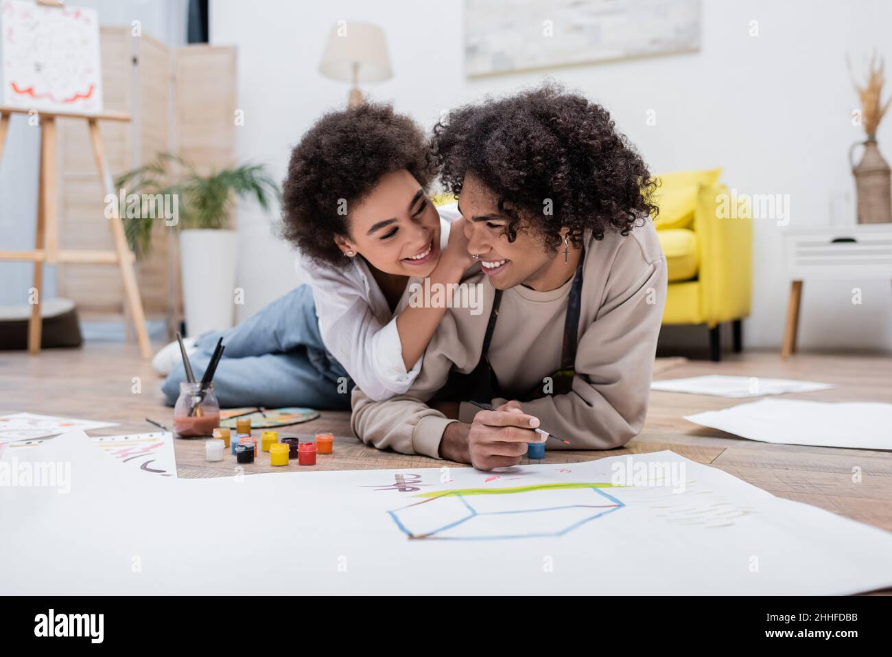 Positive african american woman hugging boyfriend with paintbrush near ...