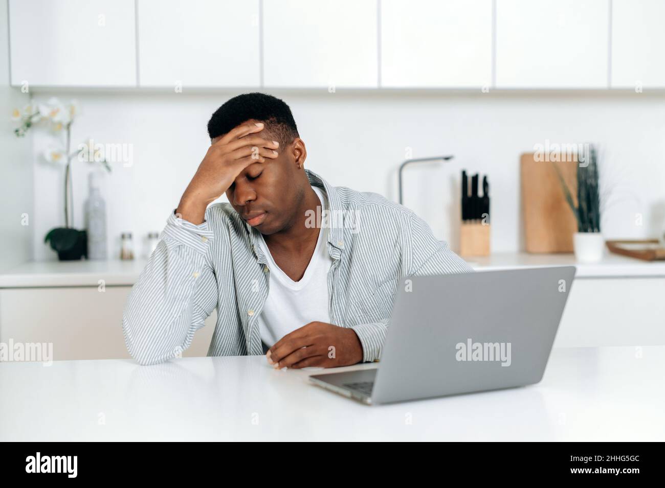 Tired dark-skinned guy in stress, freelancer, sitting at a table in ...