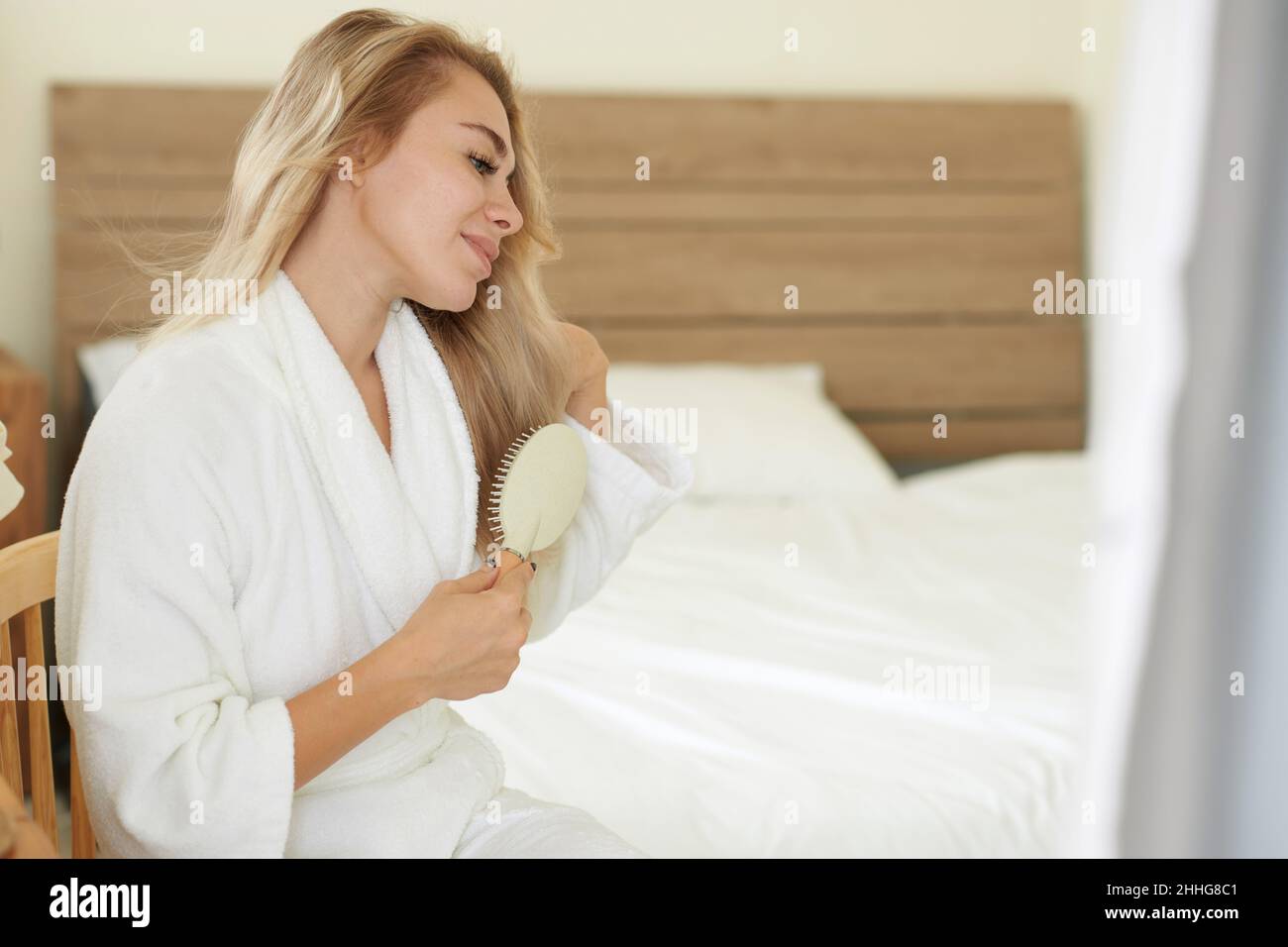 Positive young woman brushing hair in the morning after waking up Stock ...