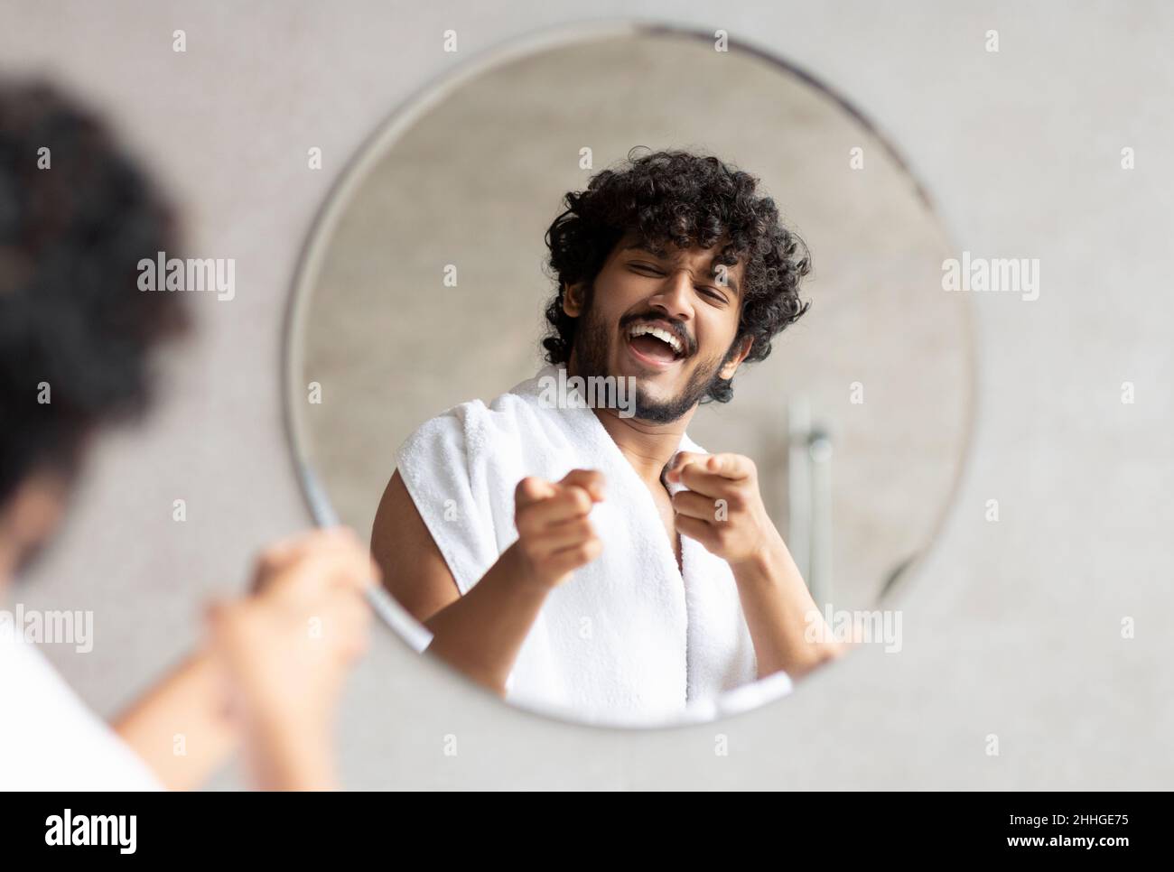 Excited indian guy pointing at mirror in bathroom with two fingers ...