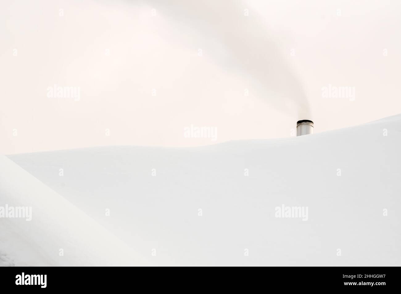 Smoke from a metal pipe on a snow-covered roof, a village house, on a ...