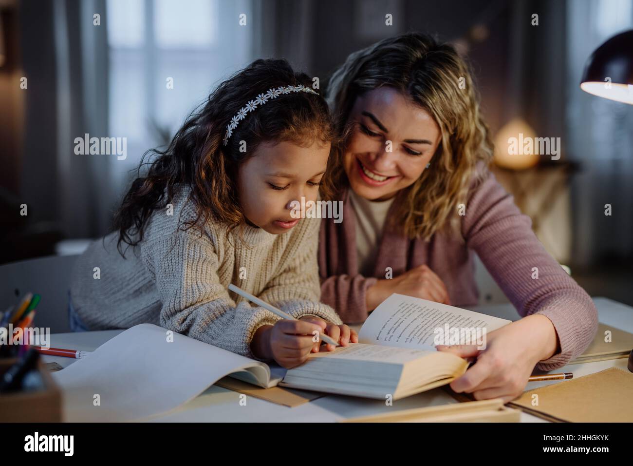 Little multiracial girl doing homework with her mother in evening at ...