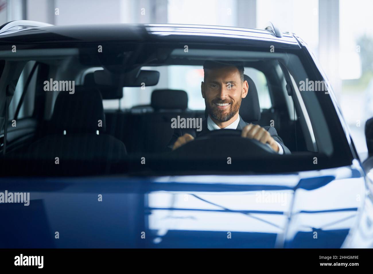 Successful businessman in suit sitting in modern auto with hands on ...