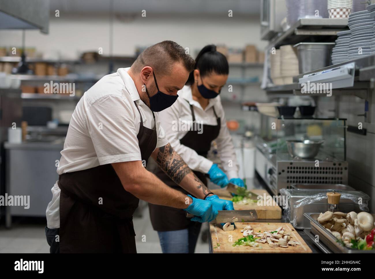 Chef and cook with face masks cutting vegetables indoors in restaurant ...