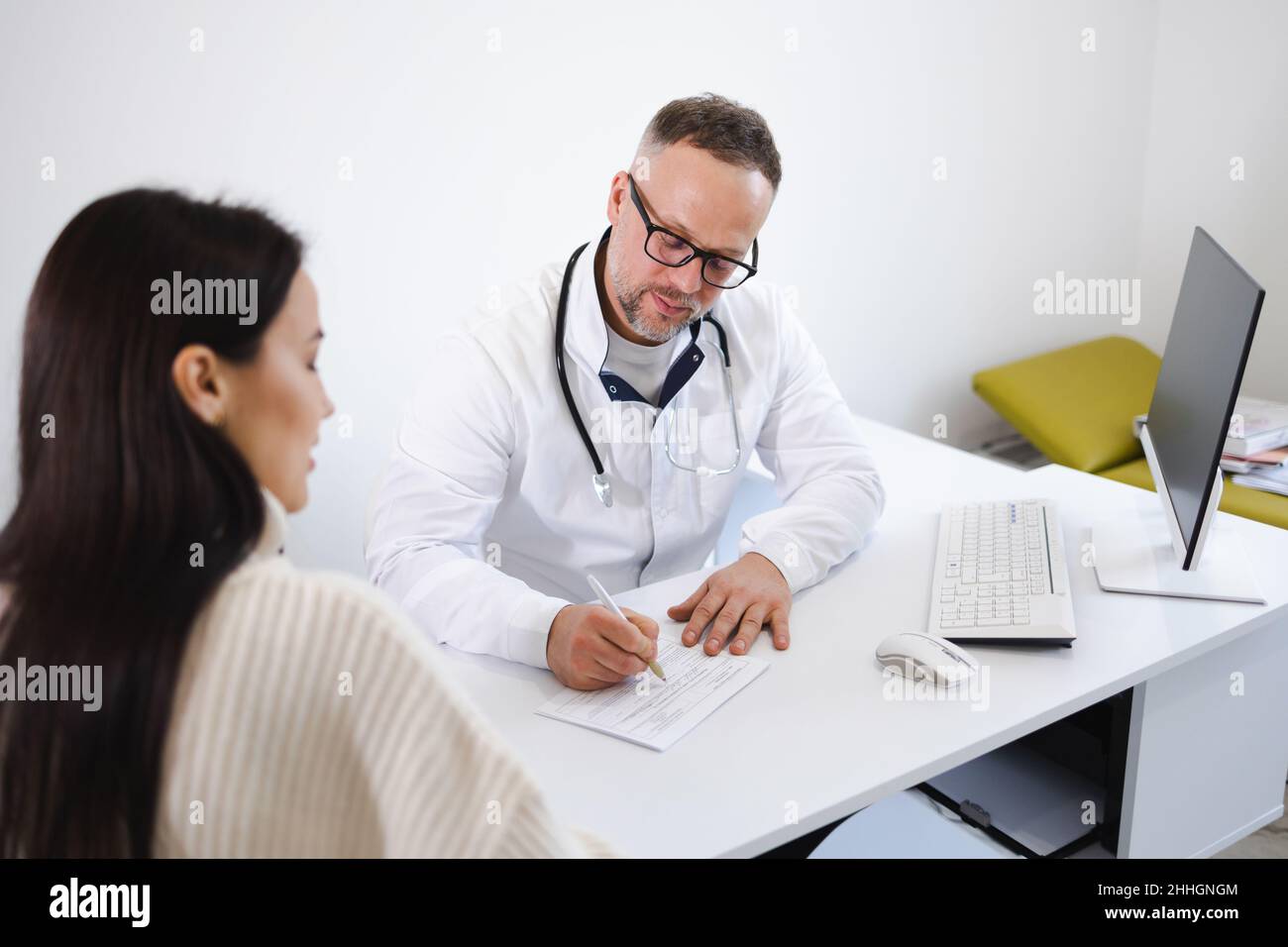 Doctor writing on a prescription note in medical office. Woman at the ...